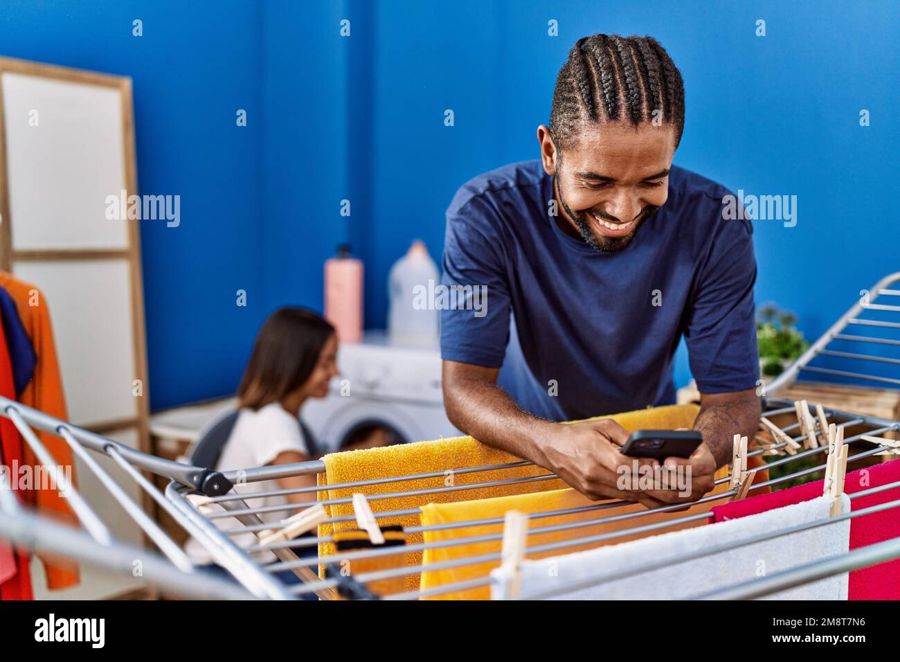 Man and woman couple using smartphone hanging clothes on clothesline at ...