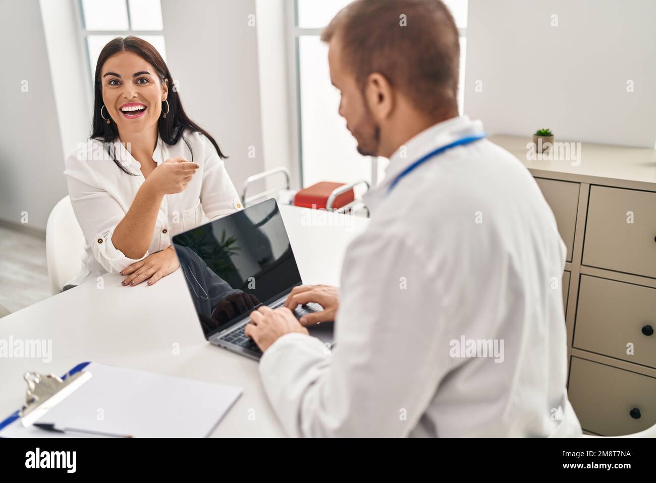 Young hispanic woman at the doctor smiling happy pointing with hand and ...