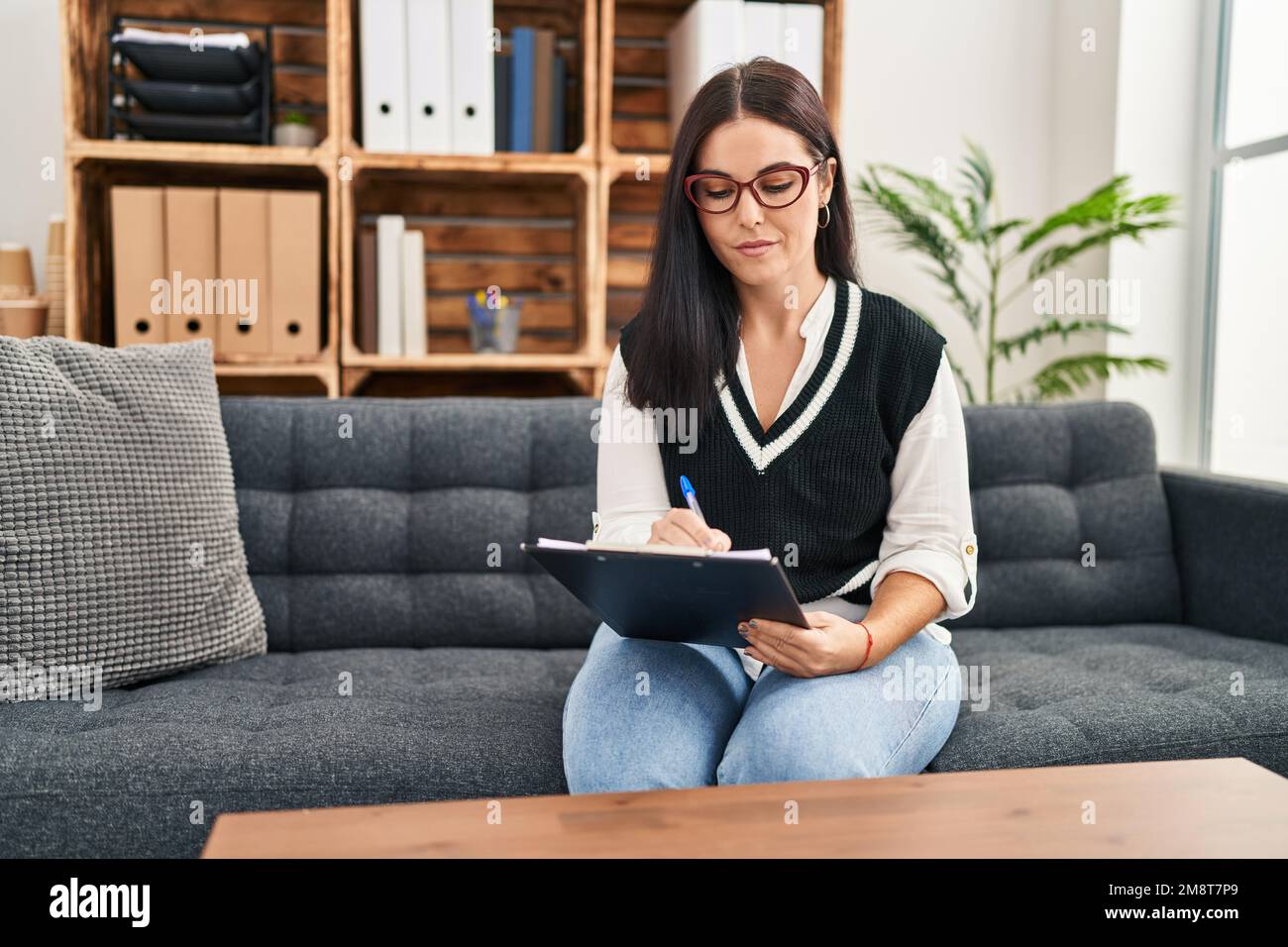 Young beautiful hispanic woman psychologist writing on document at ...
