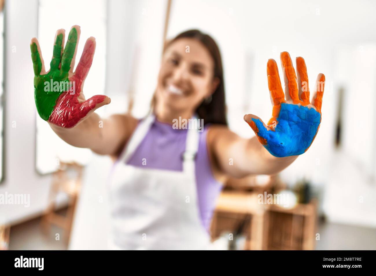 Young beautiful hispanic woman artist showing painted hands at art ...