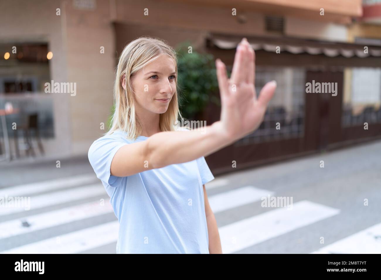 Young blonde woman doing stop gesture with hand at coffee shop terrace ...