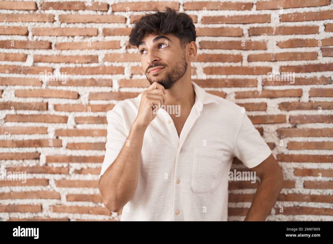 Arab man with beard standing over bricks wall background with hand on ...