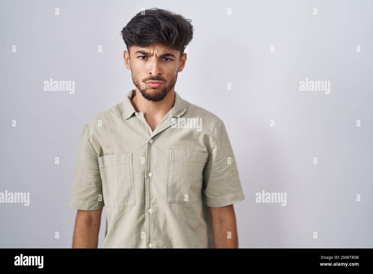Arab man with beard standing over white background skeptic and nervous ...