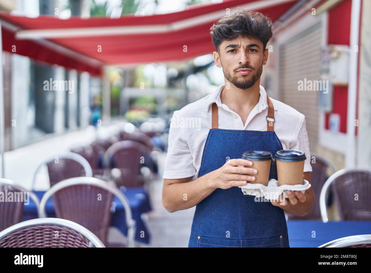 Arab man with beard wearing waiter apron at restaurant terrace thinking ...