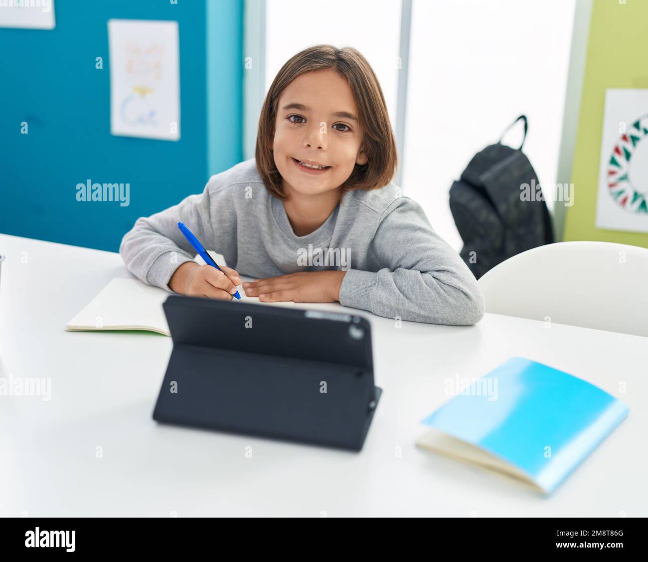 Adorable hispanic boy student sitting on table doing homework at ...