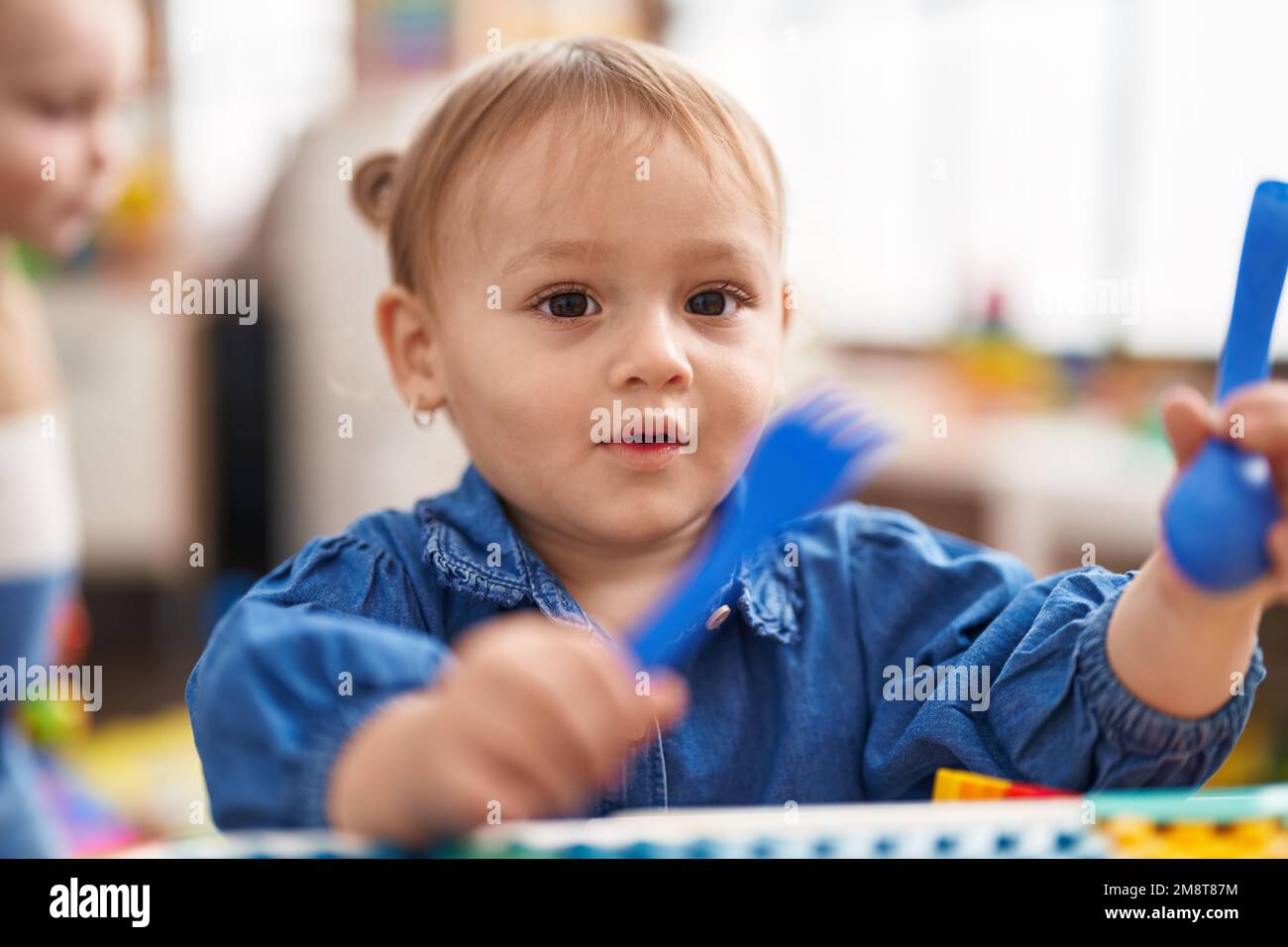 Adorable hispanic girl sitting on table holding fork and spoon at ...