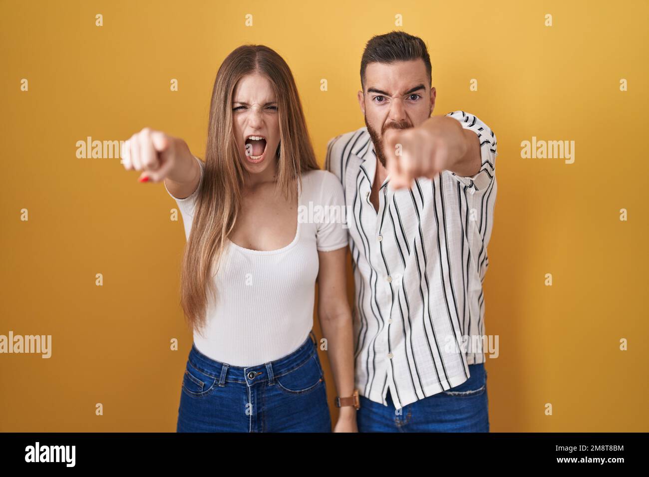 Young couple standing over yellow background pointing displeased and ...