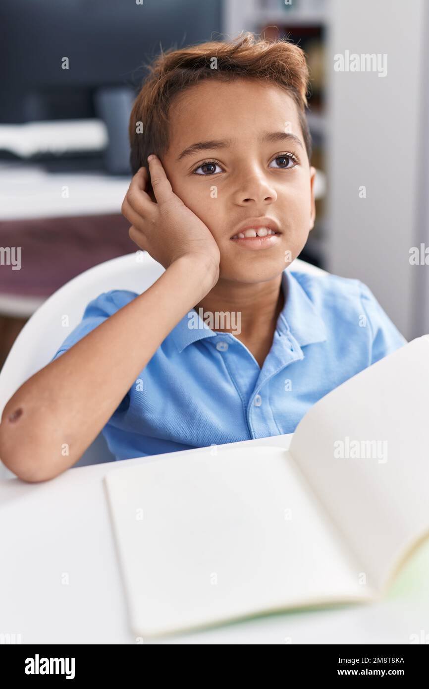 Adorable hispanic boy student reading book thinking at classroom Stock ...