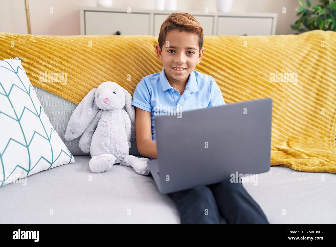 Adorable hispanic boy using laptop sitting on sofa at home Stock Photo ...