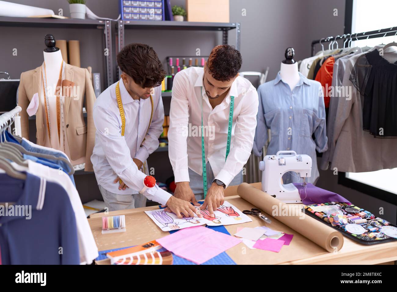Two hispanic men tailors looking clothing design speaking at atelier ...
