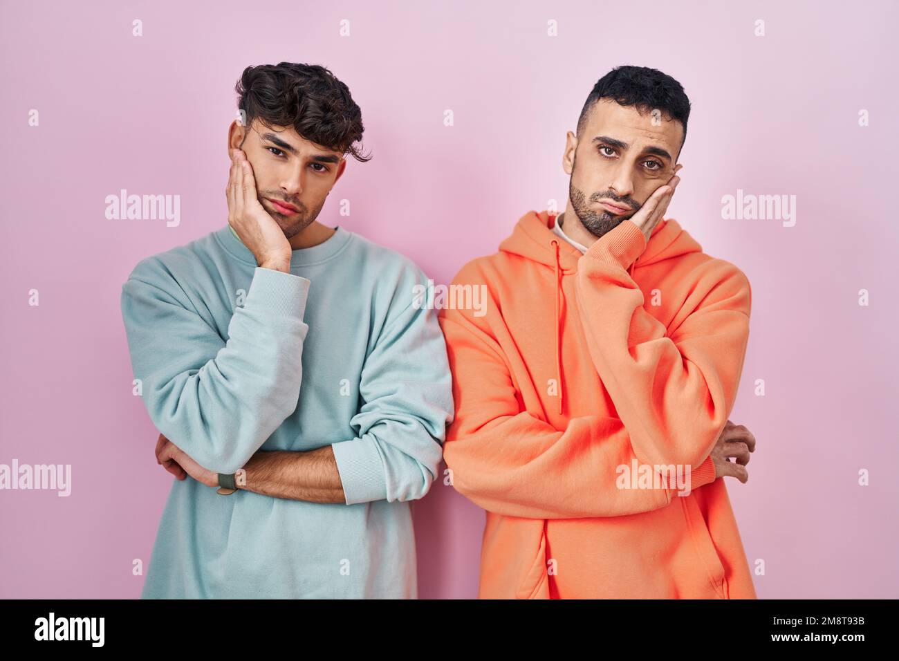 Young hispanic gay couple standing over pink background thinking ...
