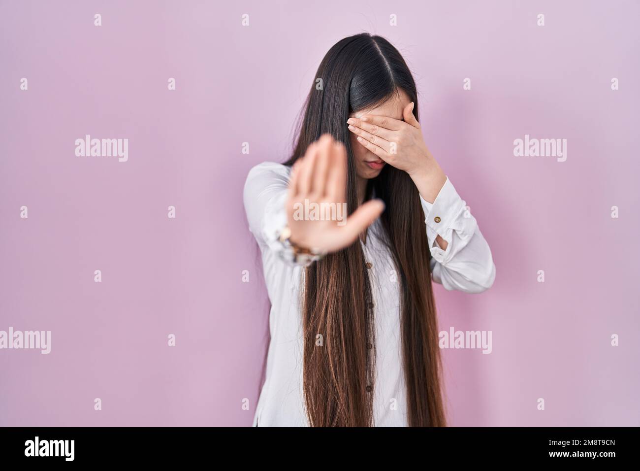 Chinese young woman standing over pink background covering eyes with ...