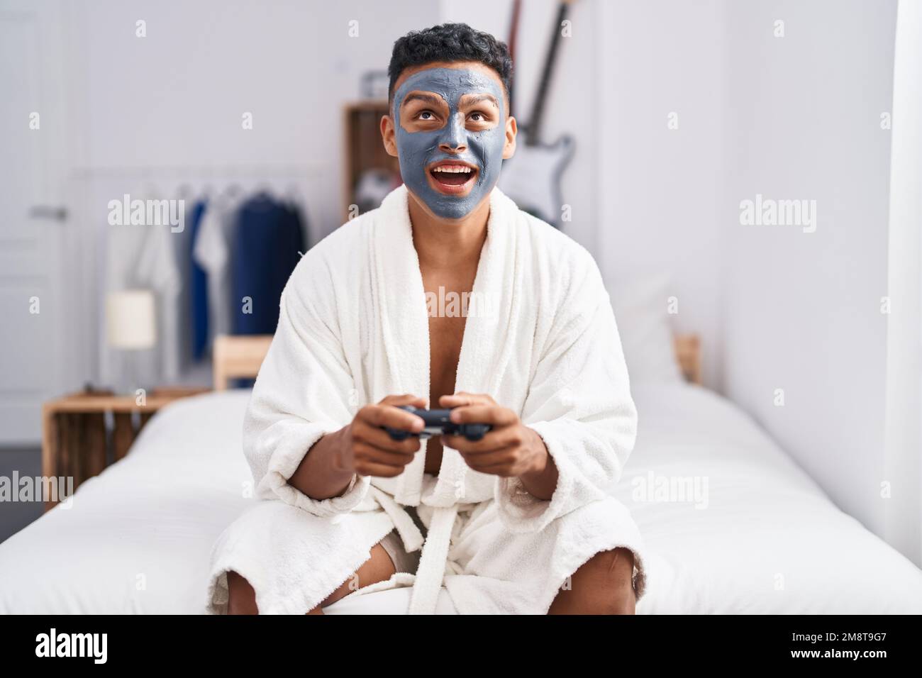 Young hispanic man wearing beauty face mask playing video games angry ...