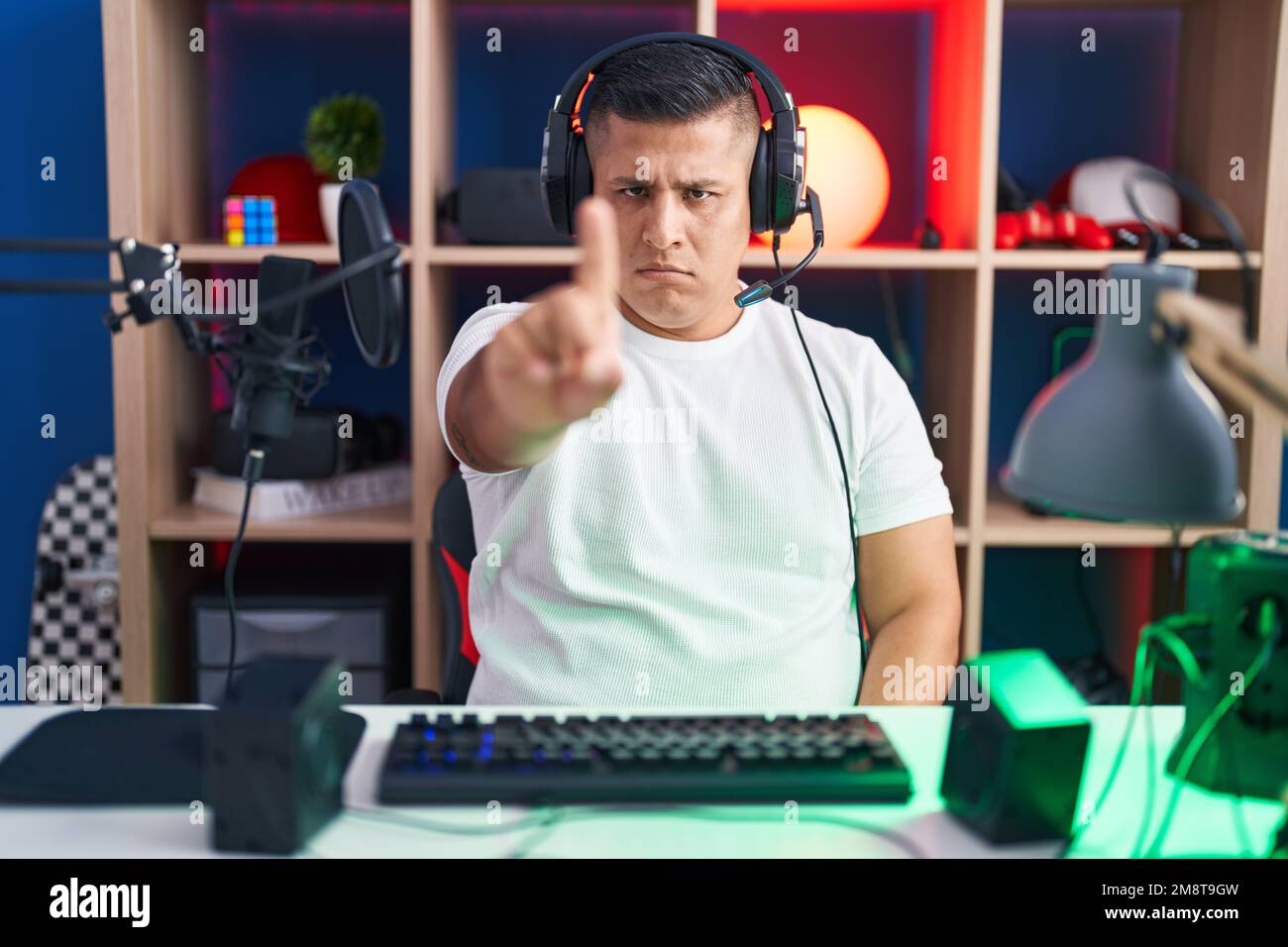 Young hispanic man playing video games pointing with finger up and ...