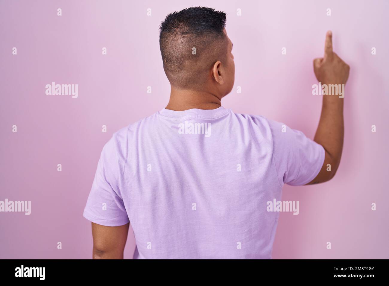 Young hispanic man standing over pink background posing backwards ...