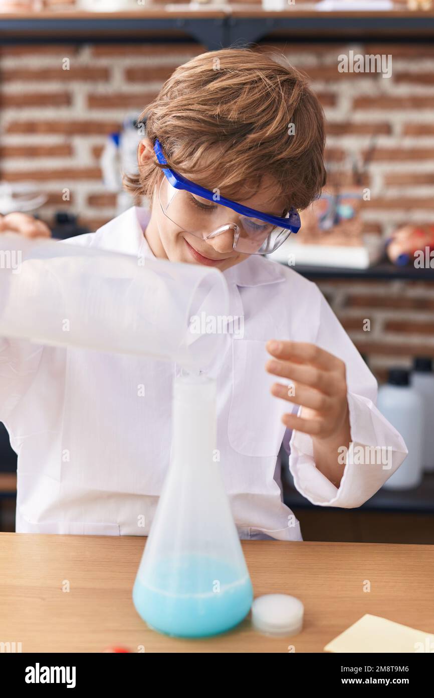 Adorable caucasian boy student pouring liquid on test tube at classroom ...
