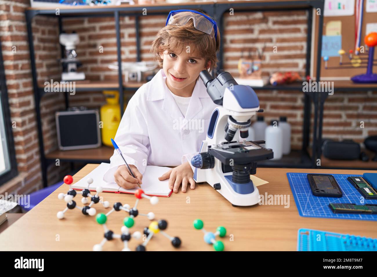 Adorable caucasian boy student using microscope writing on notebook at ...