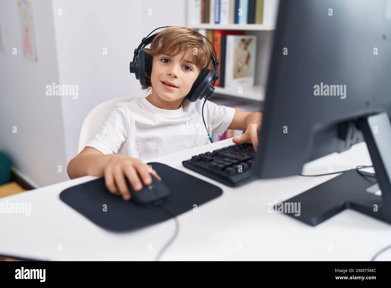 Adorable caucasian boy student using computer sitting on table at ...