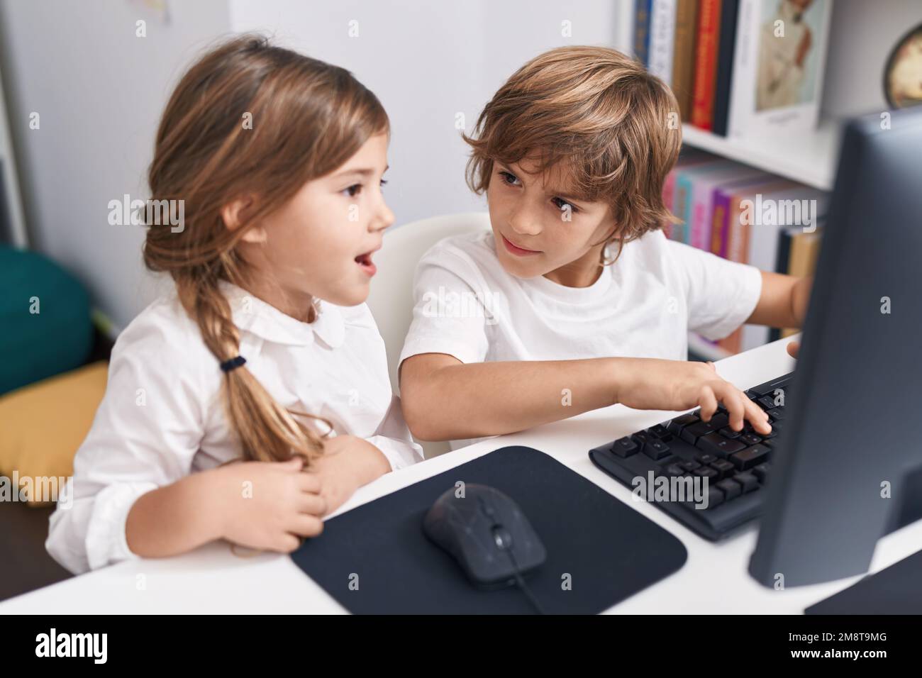 Brother and sister students using computer sitting on table at ...