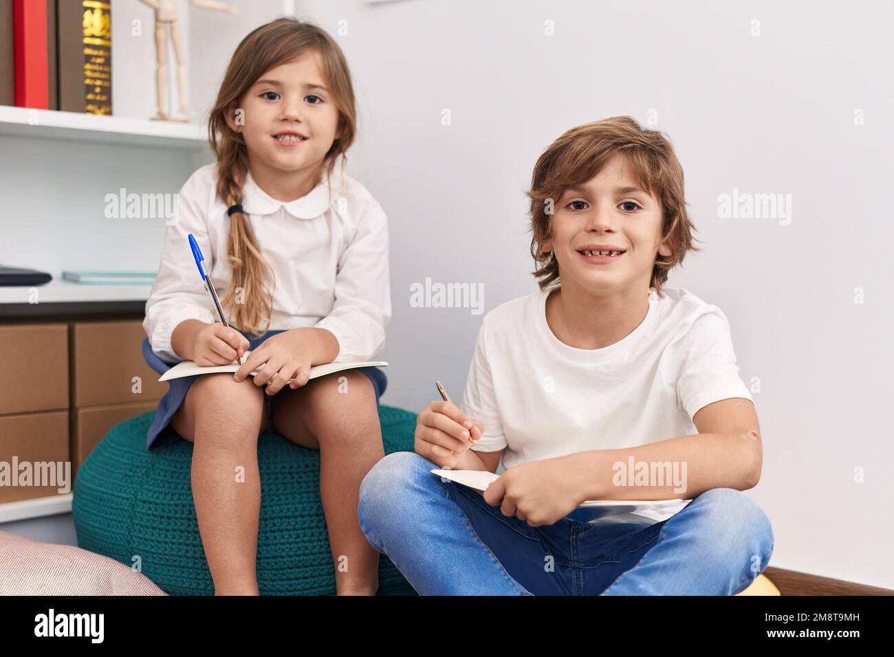 Brother and sister students writing on notebook studying at library ...