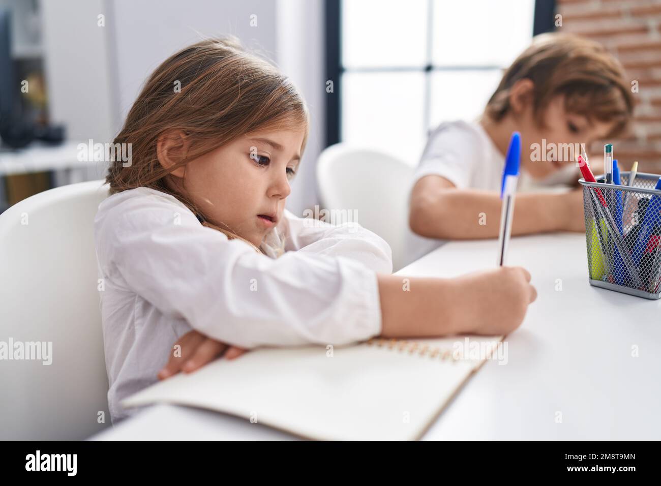 Brother and sister students writing on notebook studying at classroom ...