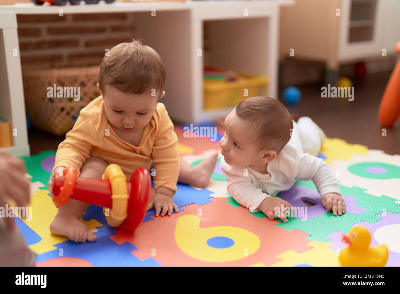 Two toddlers playing with toys sitting on floor at kindergarten Stock ...