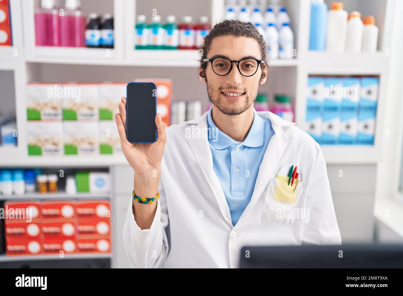 Young hispanic man working at pharmacy drugstore showing smartphone ...