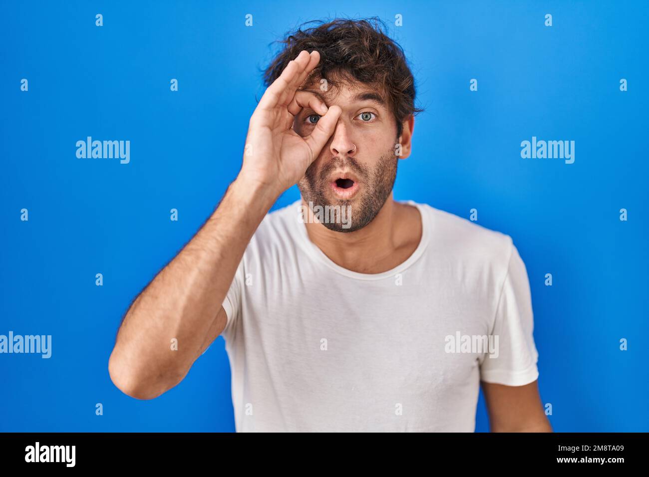 Hispanic young man standing over blue background doing ok gesture ...