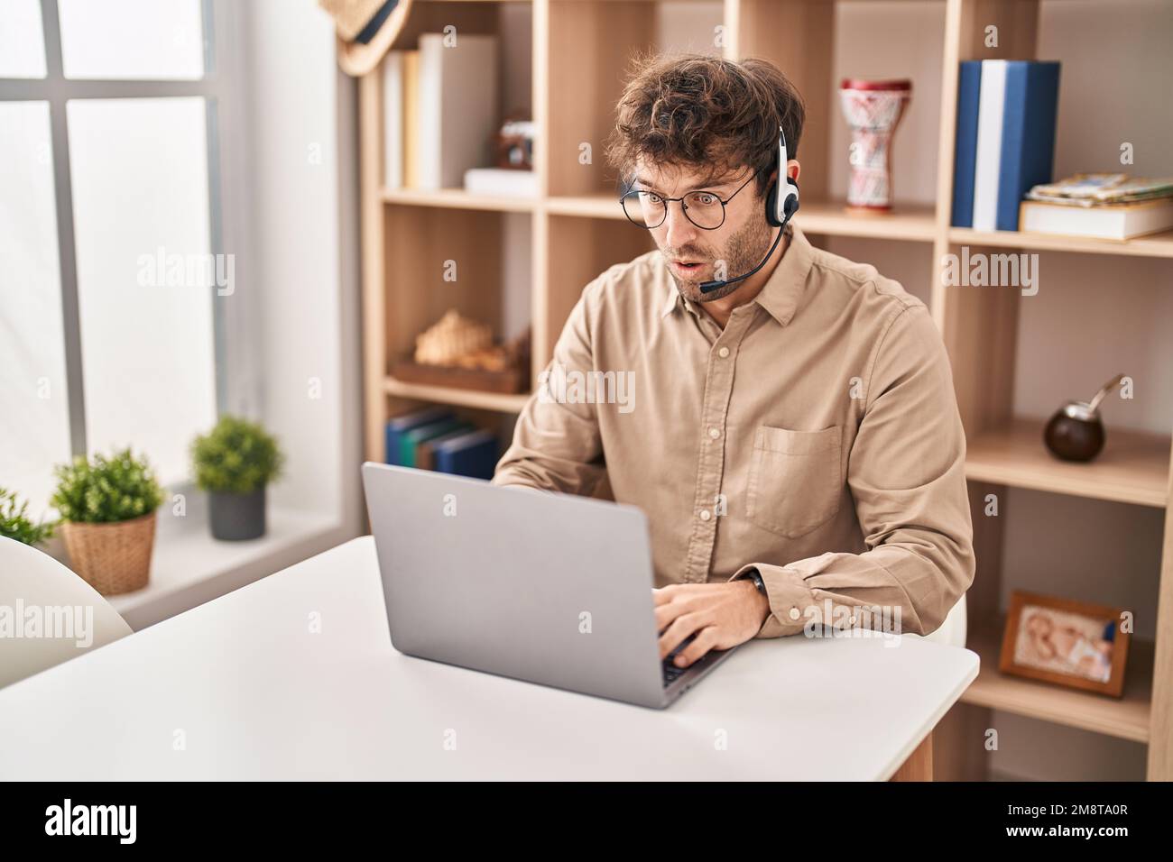 Hispanic young man wearing call center agent headset scared and amazed ...