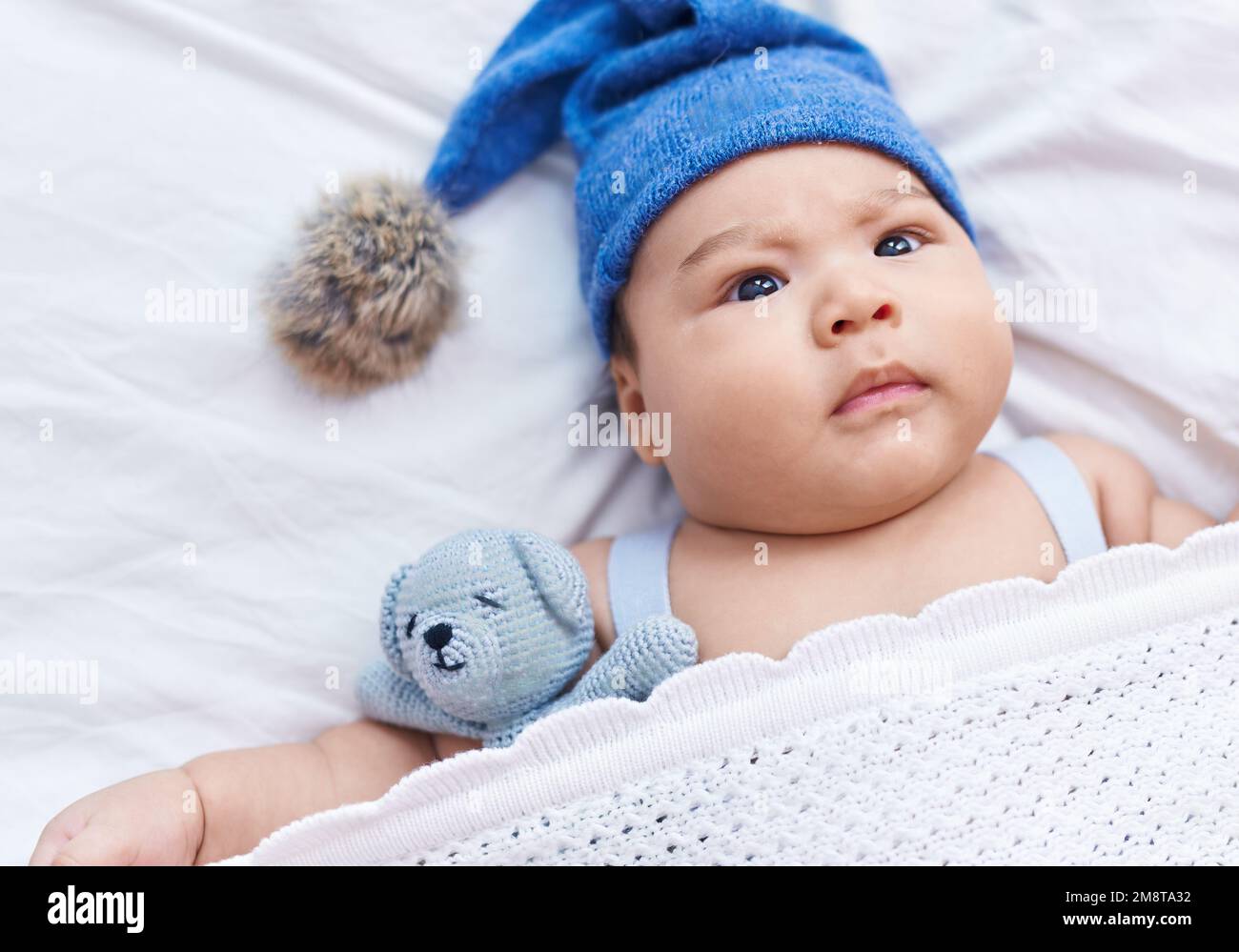 Adorable hispanic toddler wearing wool cap lying on bed at bedroom ...