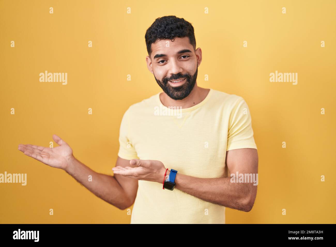Hispanic man with beard standing over yellow background inviting to ...