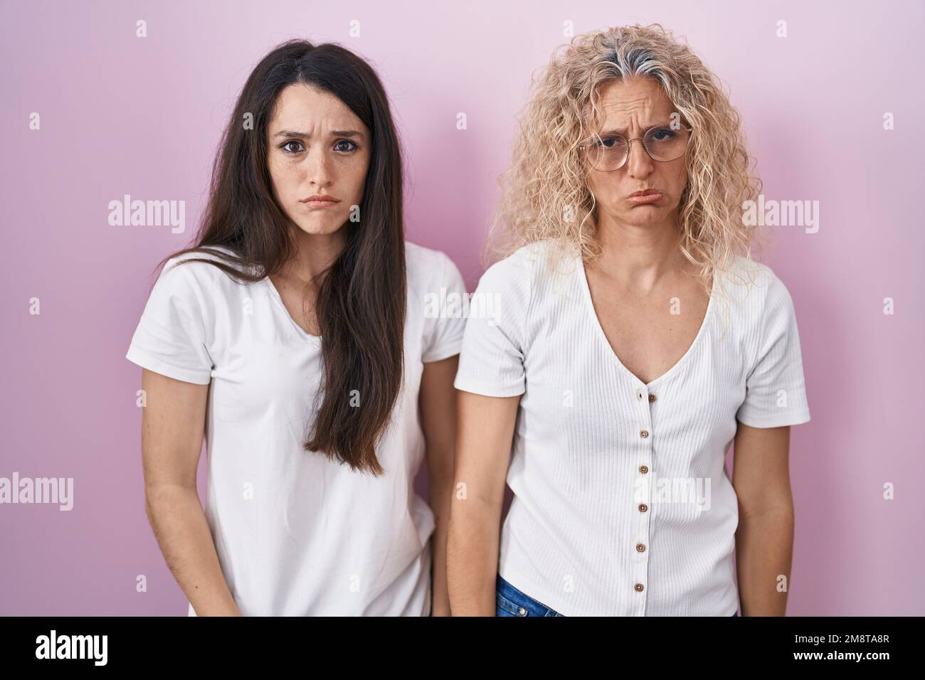 Mother and daughter standing together over pink background depressed ...