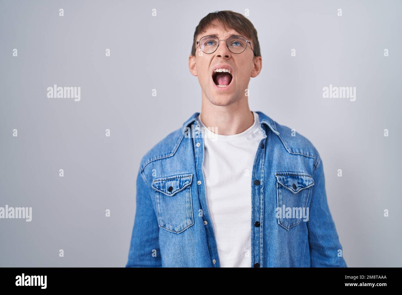 Caucasian blond man standing wearing glasses angry and mad screaming ...