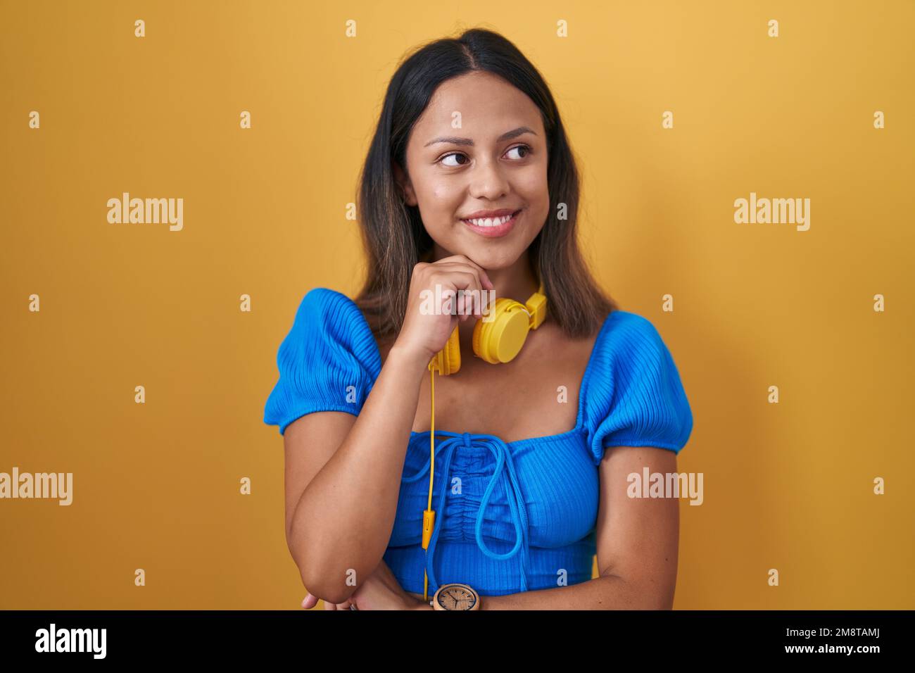 Hispanic young woman standing over yellow background with hand on chin ...