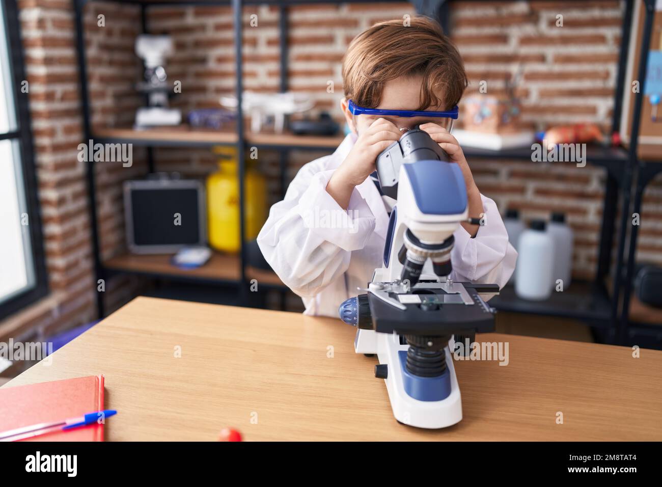 Adorable hispanic boy student using microscope at laboratory classroom ...