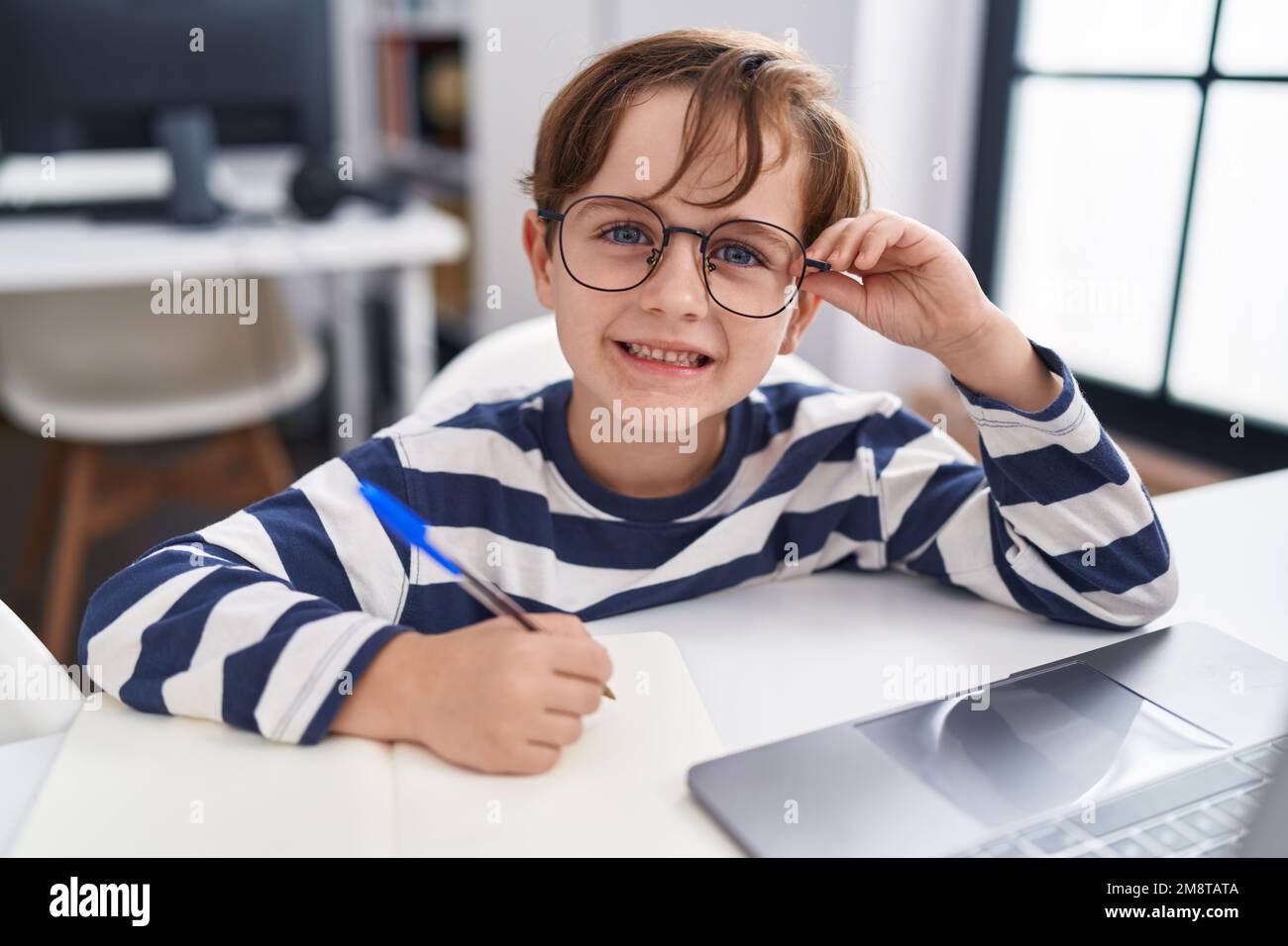 Adorable hispanic boy student using computer writing on notebook at ...