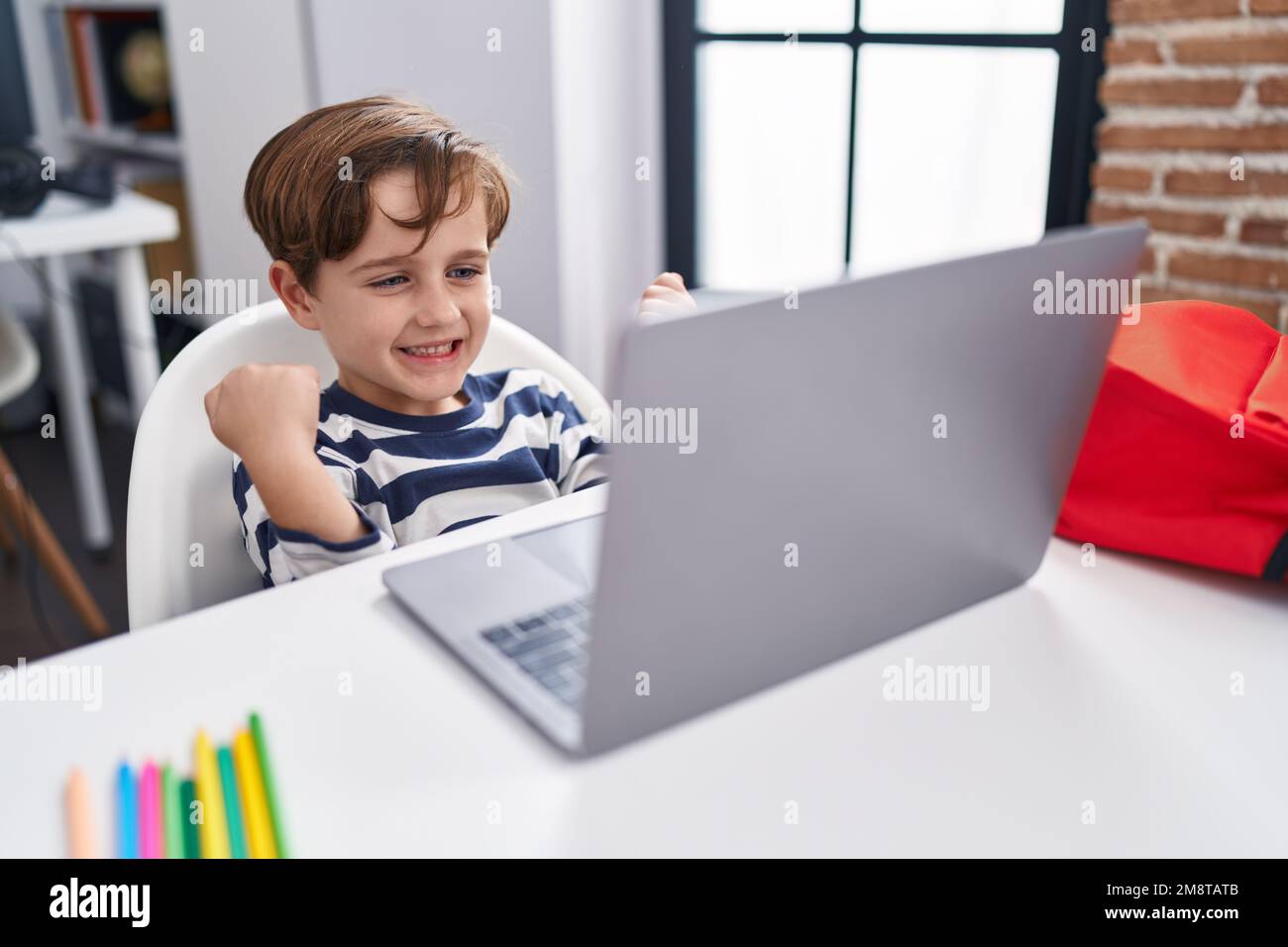 Adorable hispanic boy student using laptop with cheerful expression at ...