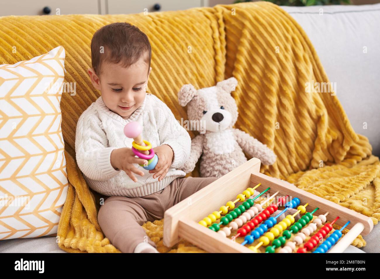 Adorable hispanic toddler playing with abacus sitting on sofa at home ...
