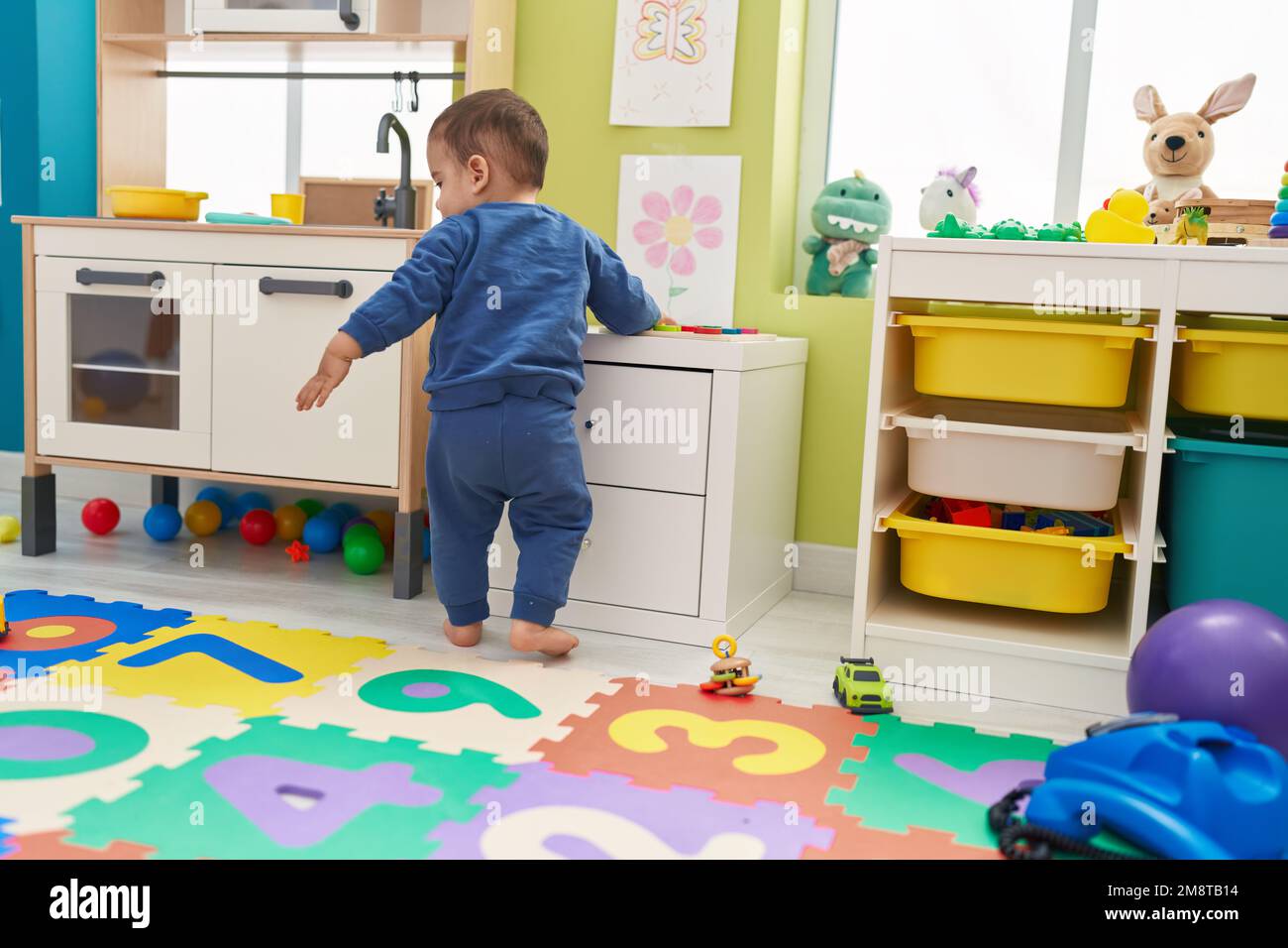 Adorable hispanic toddler playing with play kitchen standing at ...