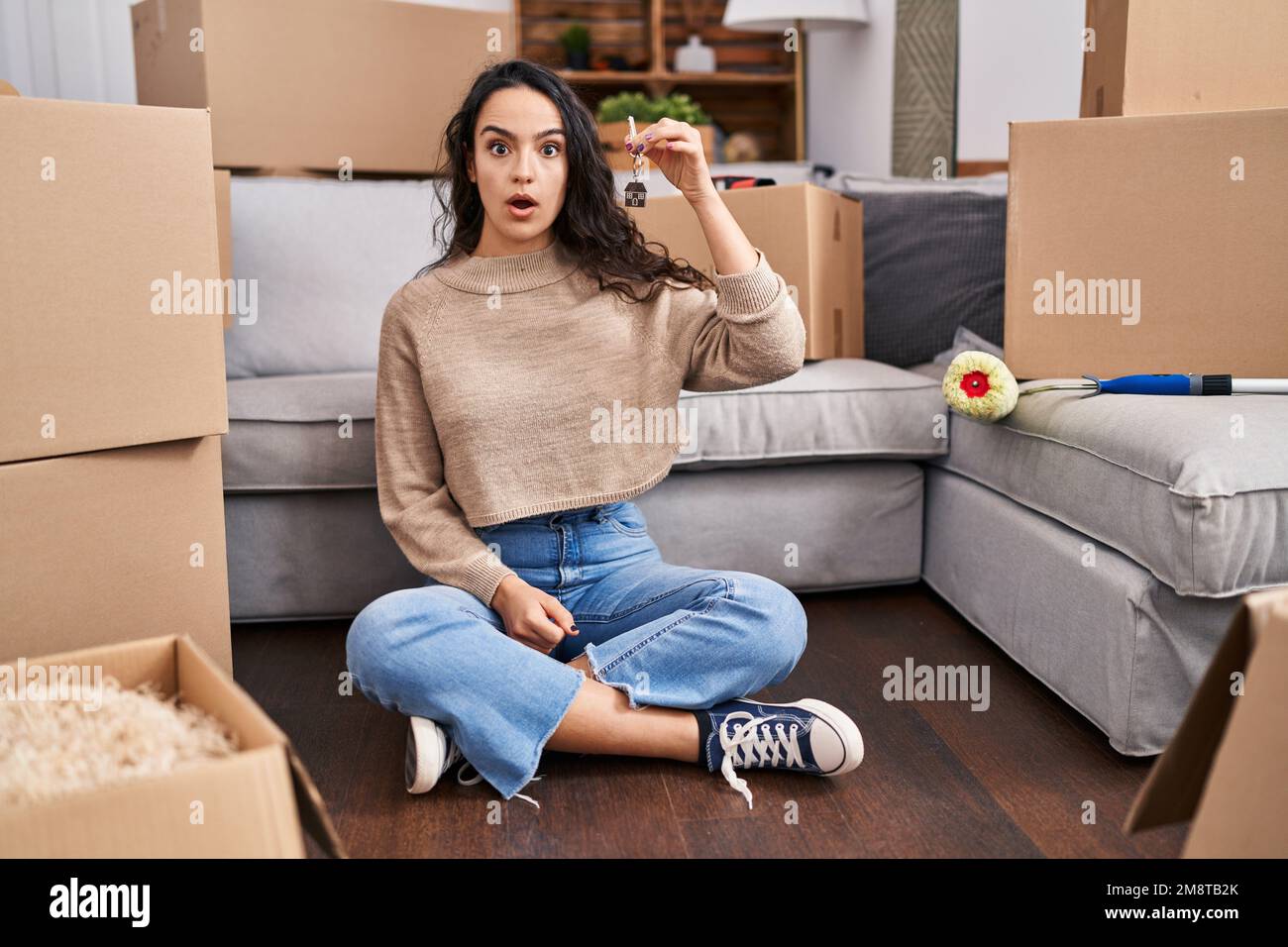 Young brunette woman sitting on the floor at new home holding keys ...