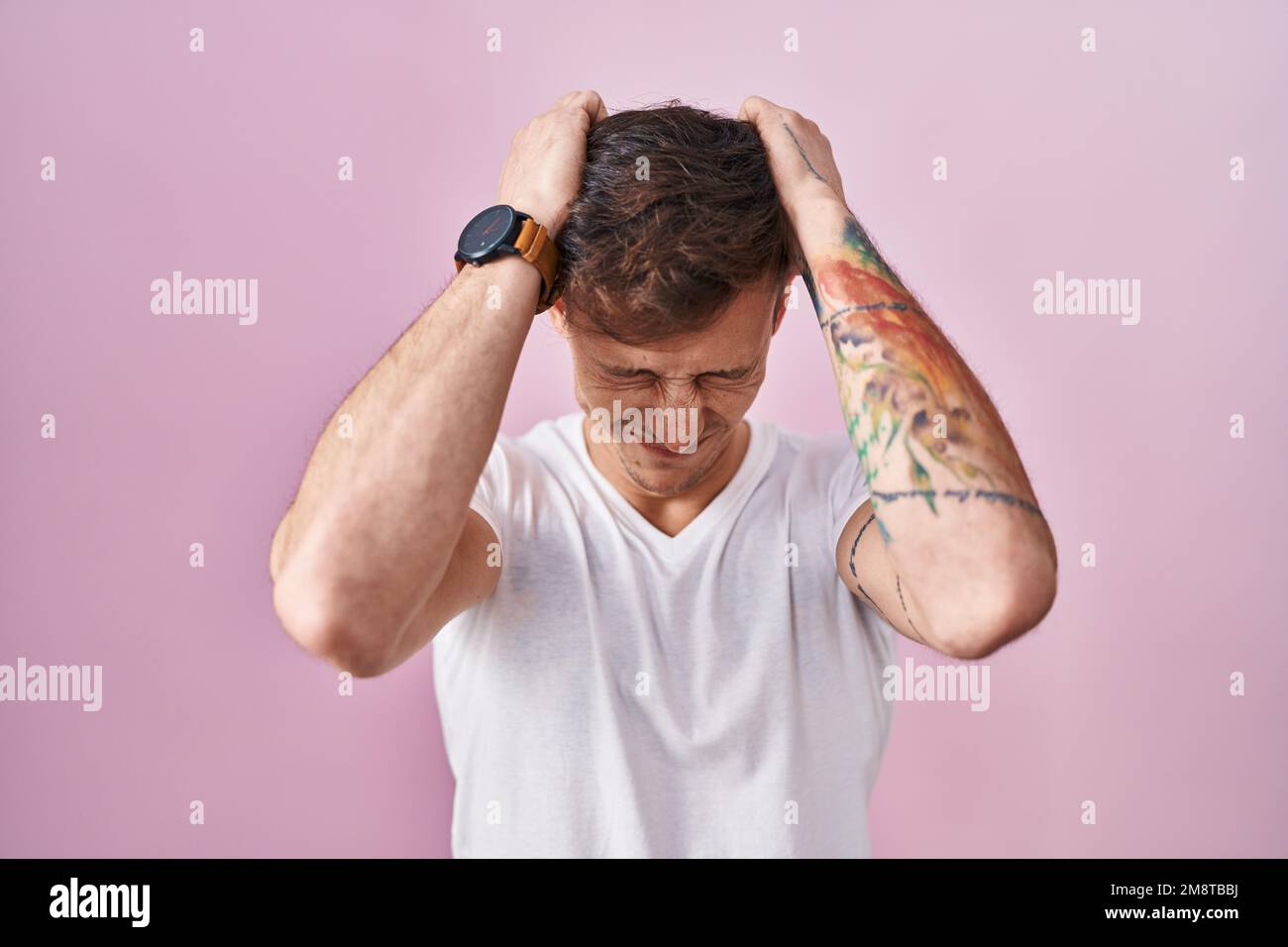 Caucasian man standing over pink background suffering from headache ...