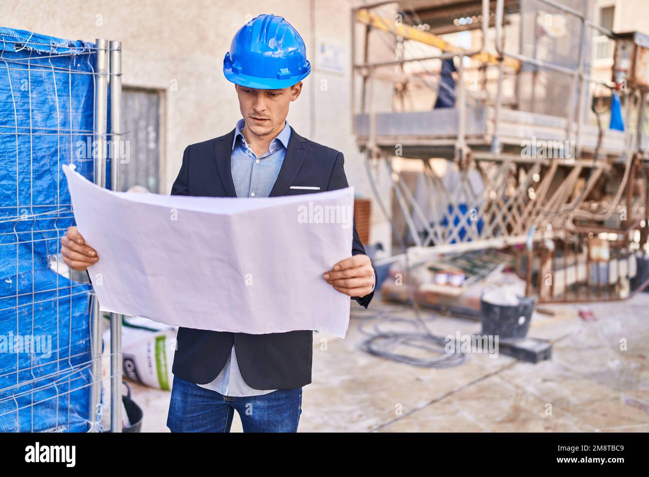 Young man architect standing with relaxed expression looking blueprint ...