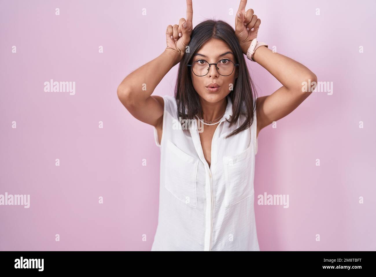Brunette young woman standing over pink background wearing glasses ...