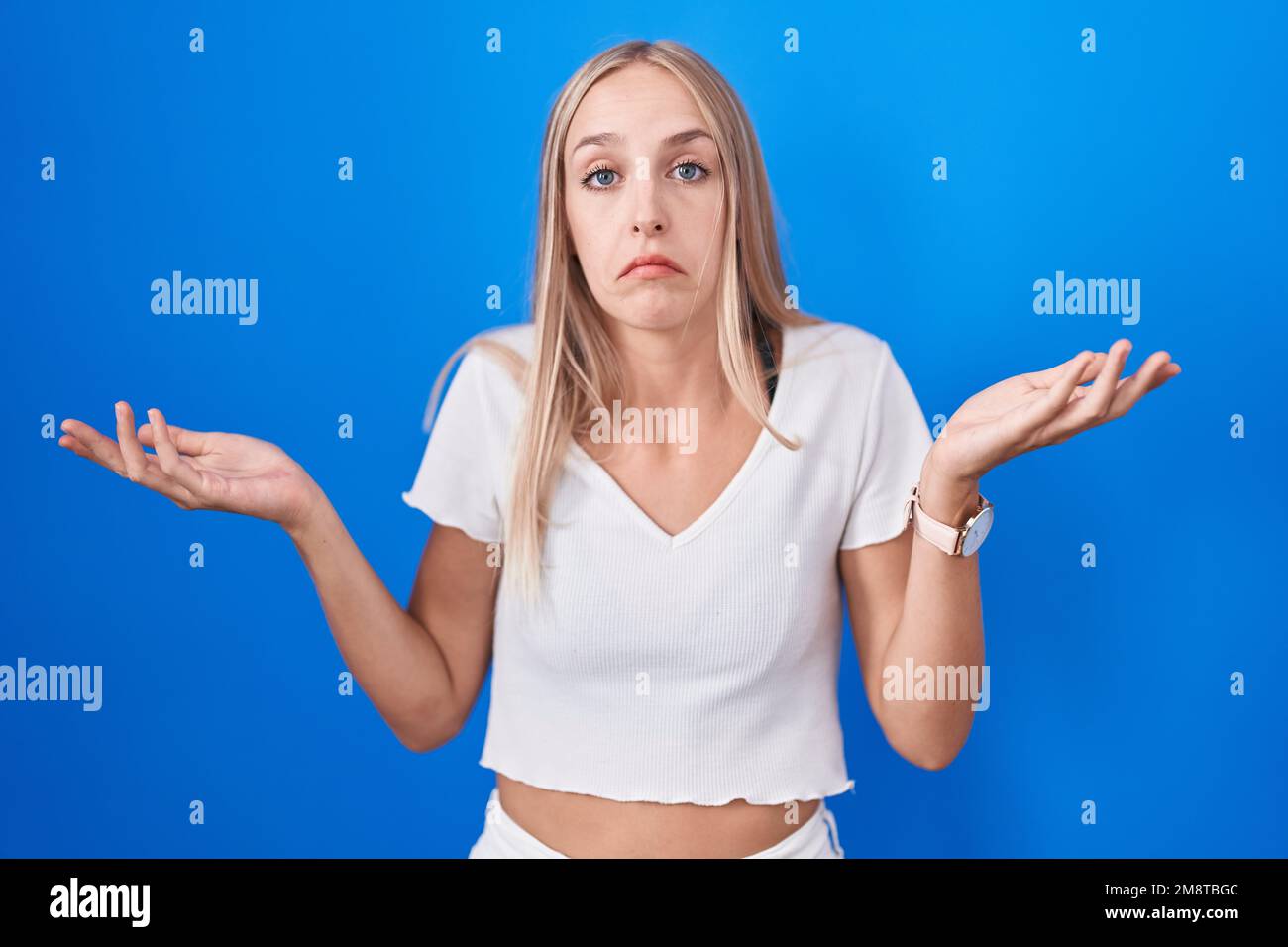 Young caucasian woman standing over blue background clueless and ...