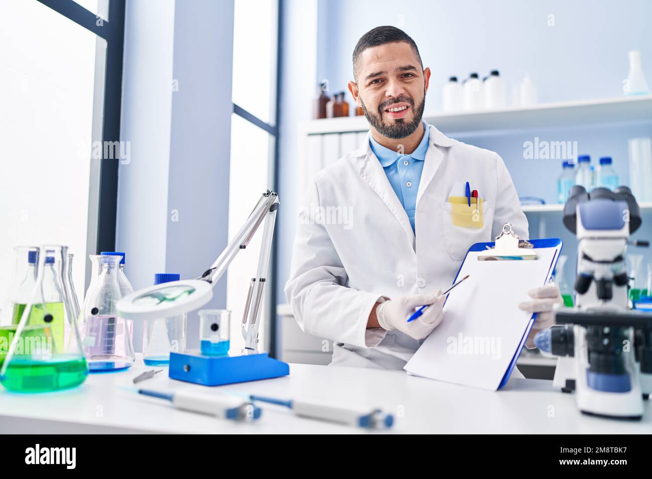 Hispanic man working at scientist laboratory holding blank clipboard ...
