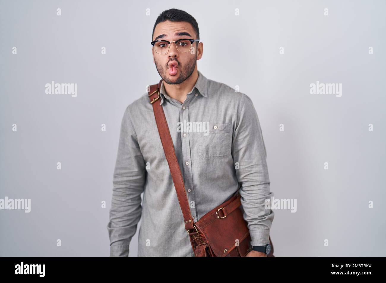 Young hispanic man wearing suitcase making fish face with lips, crazy ...