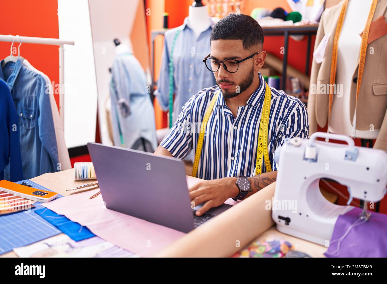 Young latin man tailor using laptop at atelier Stock Photo - Alamy