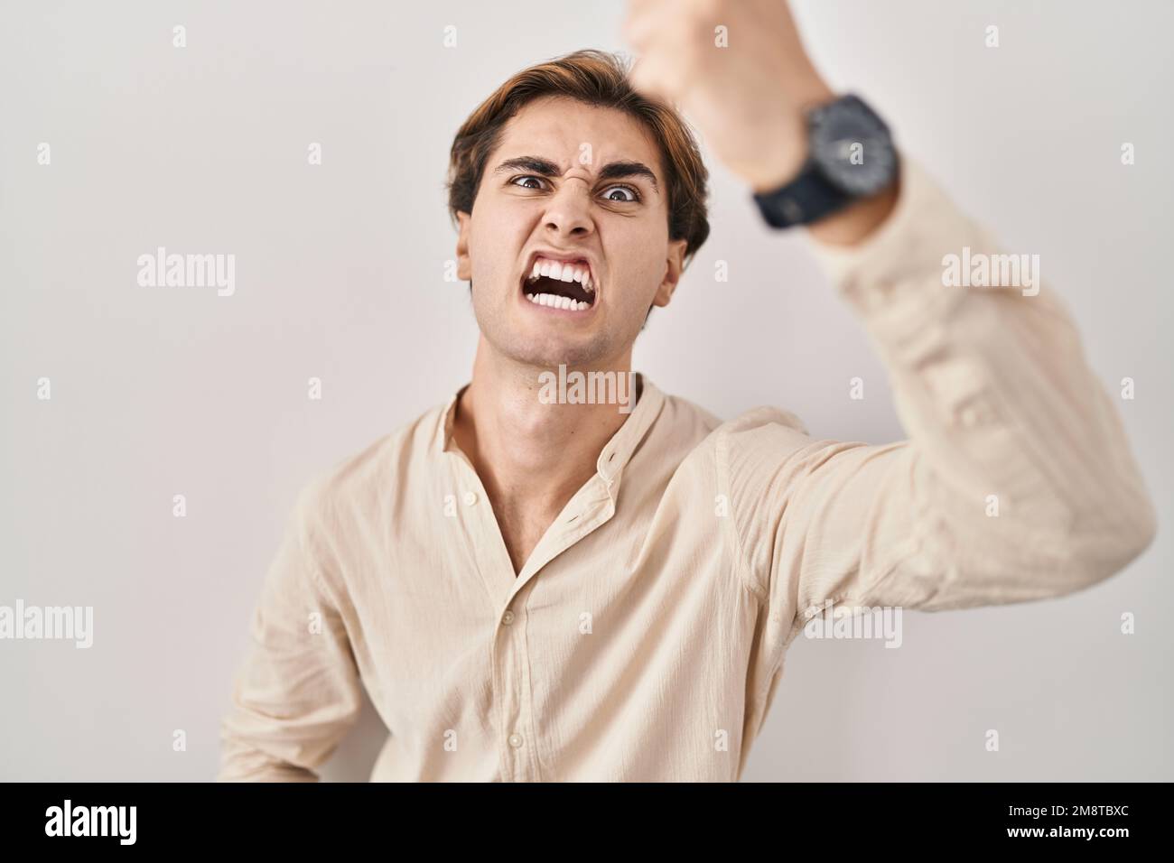 Young man standing over isolated background angry and mad raising fist ...