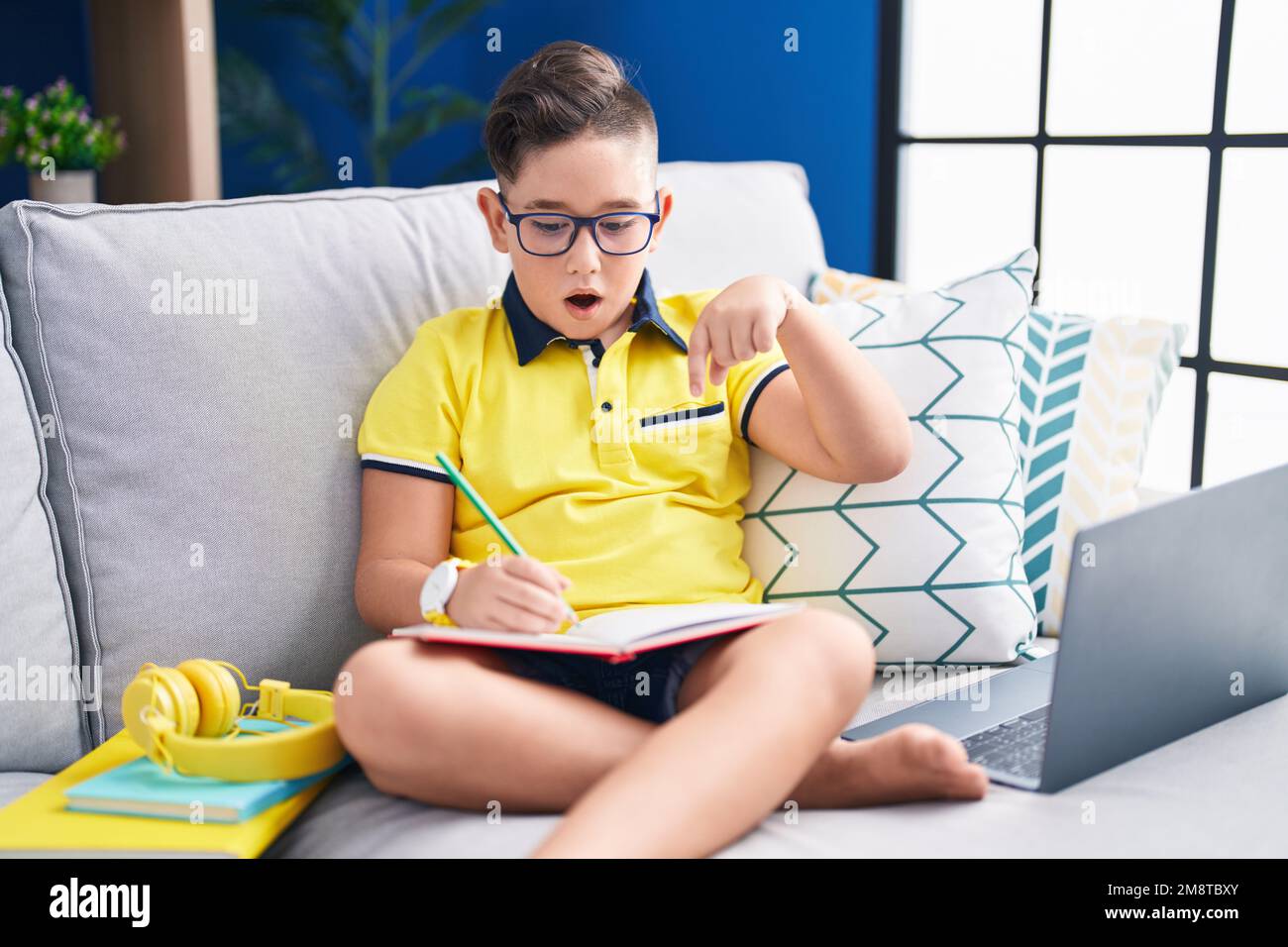 Young hispanic kid doing homework sitting on the sofa pointing down ...