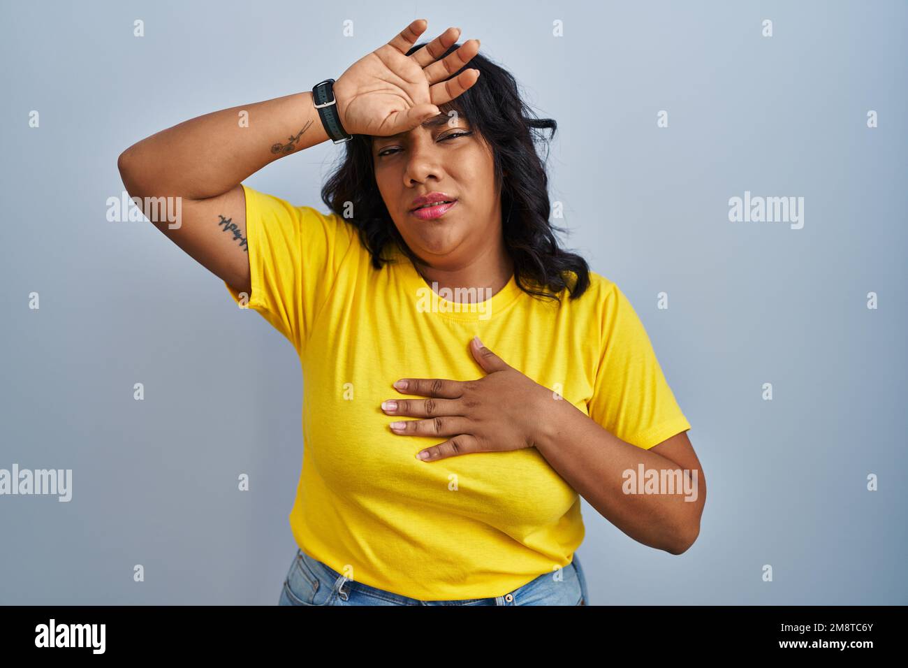 Hispanic woman standing over blue background touching forehead for ...